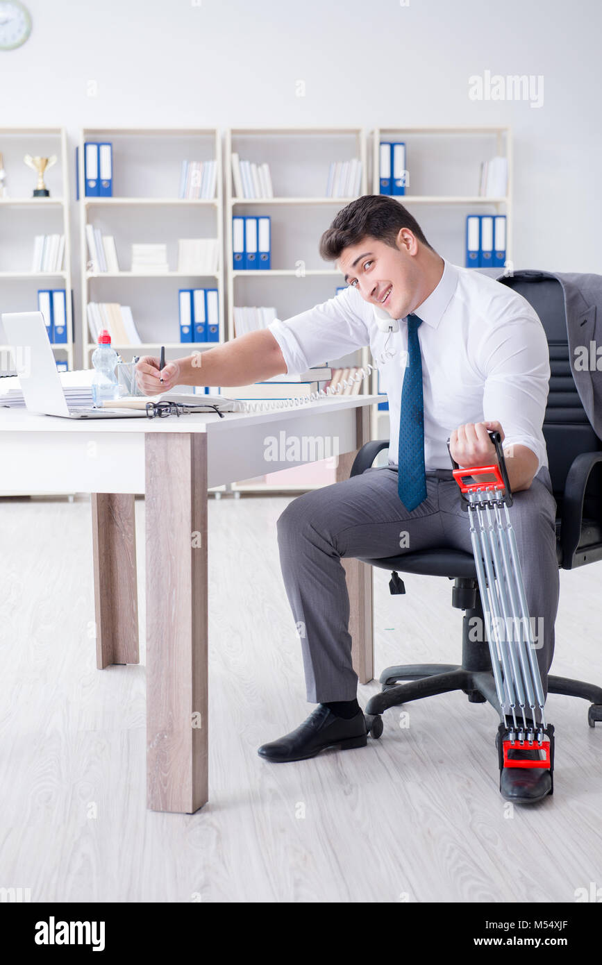 The young businessman exercising with elastic expander in office Stock ...