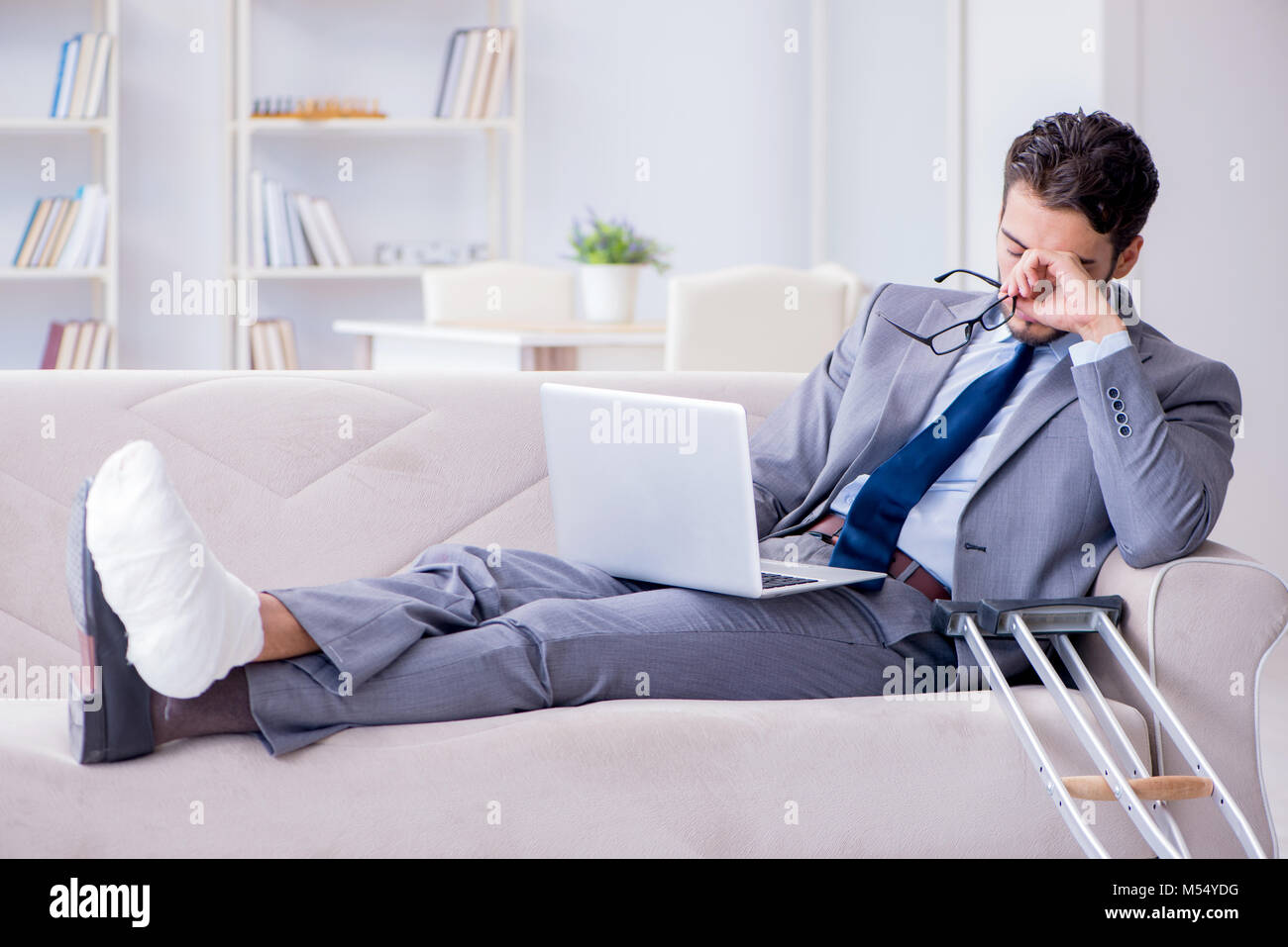 The businessman with crutches and broken leg at home working Stock ...