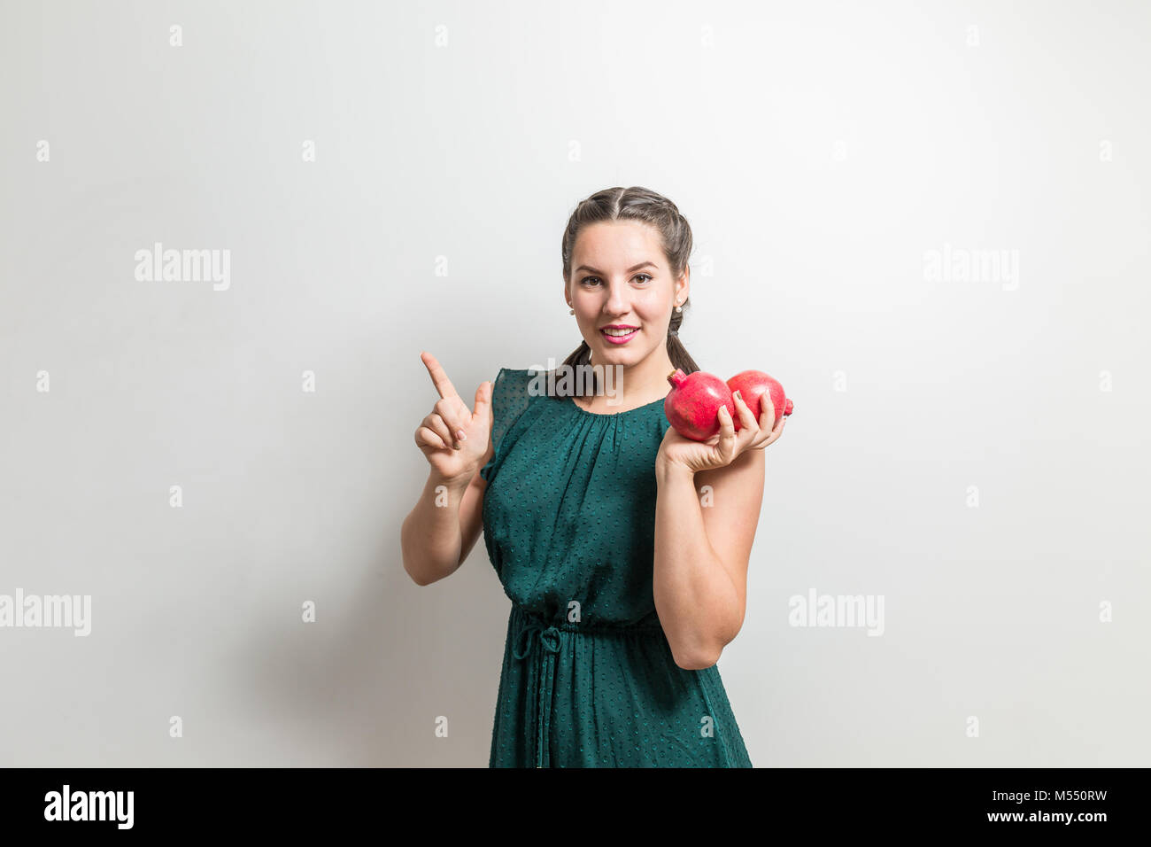 Young girl looks in camera and points to side while holding fruits ...