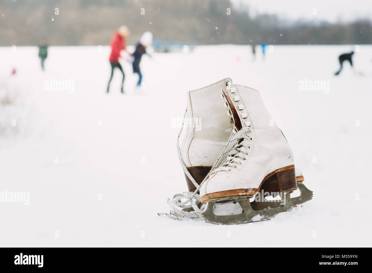 A pair of female ice skates lying on the snow with skaters in the ...