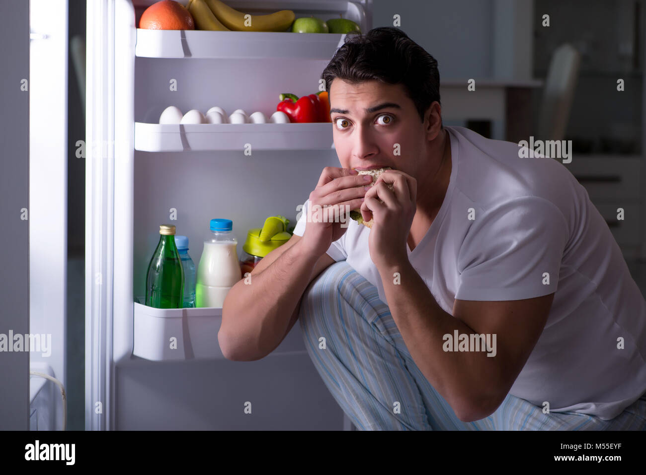 Man at the fridge eating at night Stock Photo - Alamy