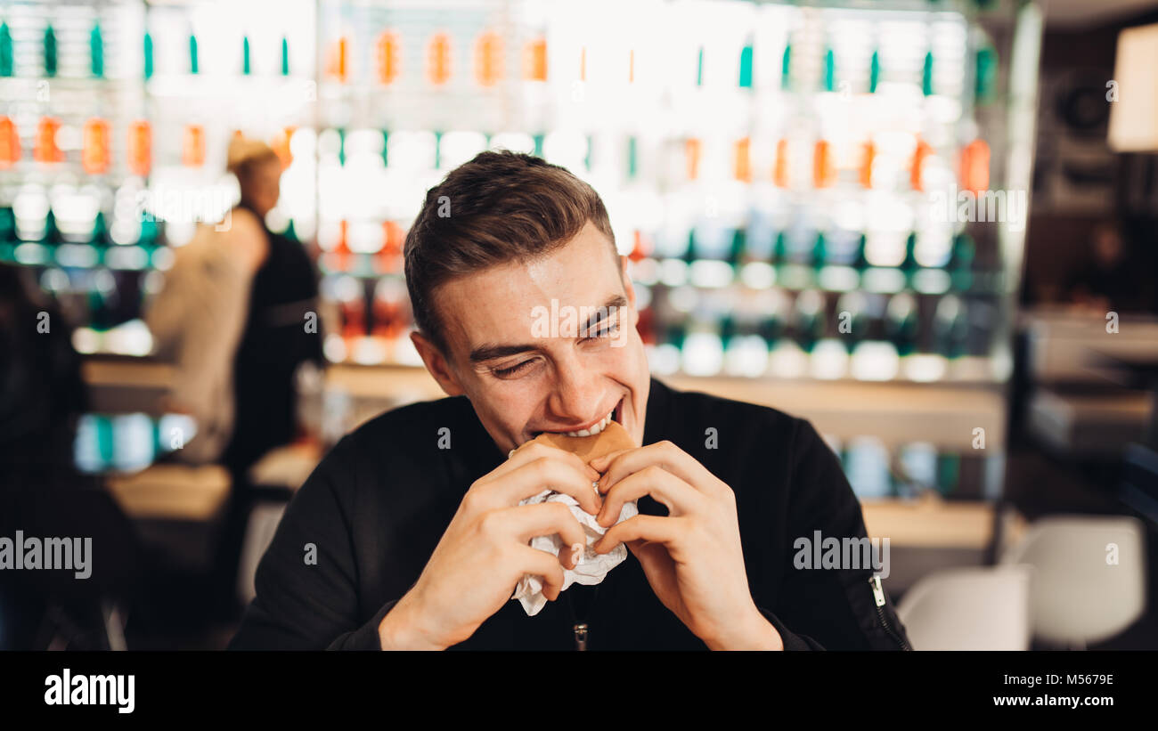 Young man eating fatty hamburger.Craving fast food.Enjoying guilty ...
