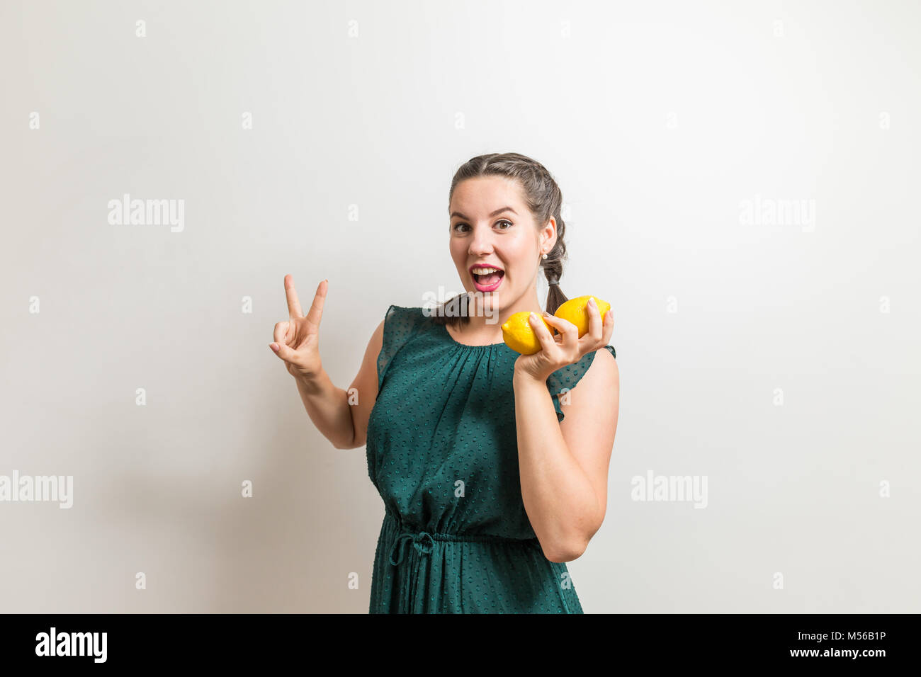 Charming girl shows peace sign with fingers and holds lemons Stock ...