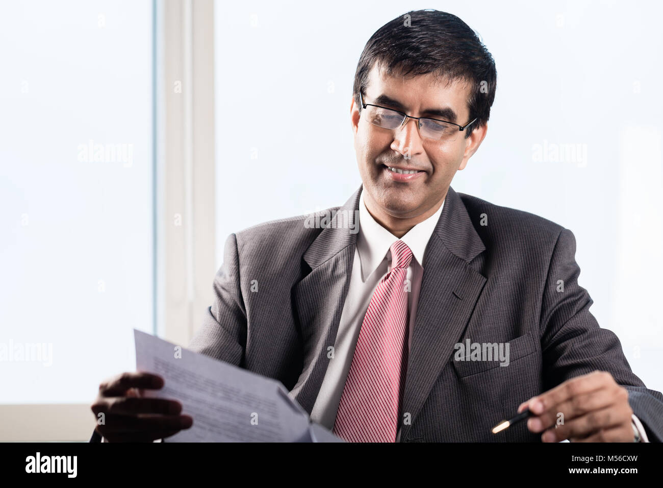 Indian Senior Executive in his skyscraper office, reading business ...