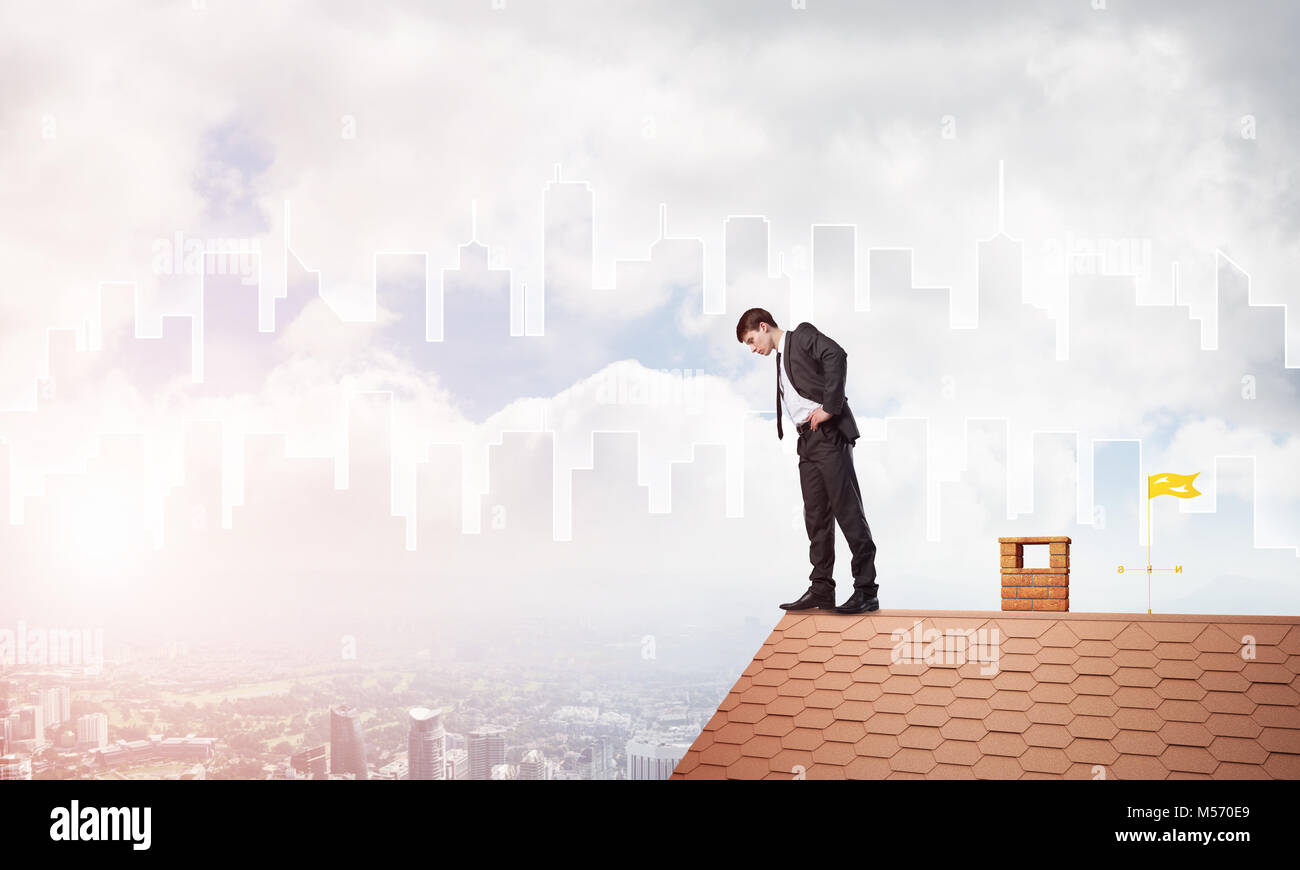 Businessman looking down from roof and modern cityscape at background ...