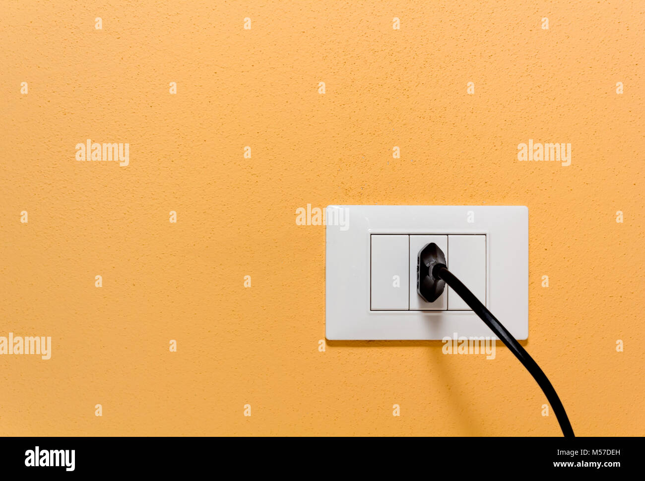 Black plug inserted in a wall socket on an orange interior wall Stock ...