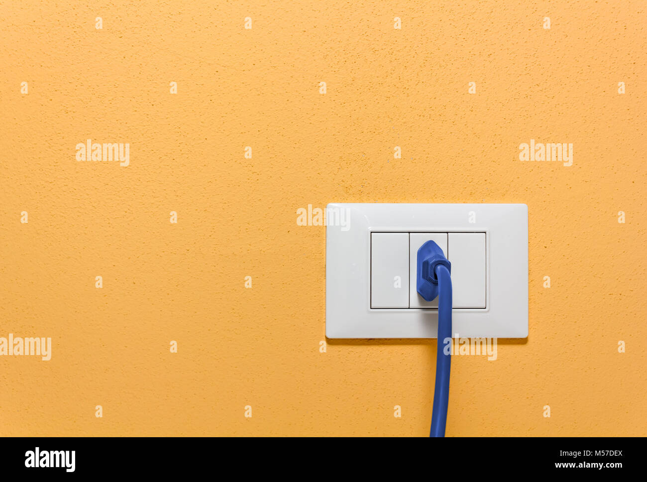 Blue plug inserted in a wall socket on an orange interior wall Stock ...