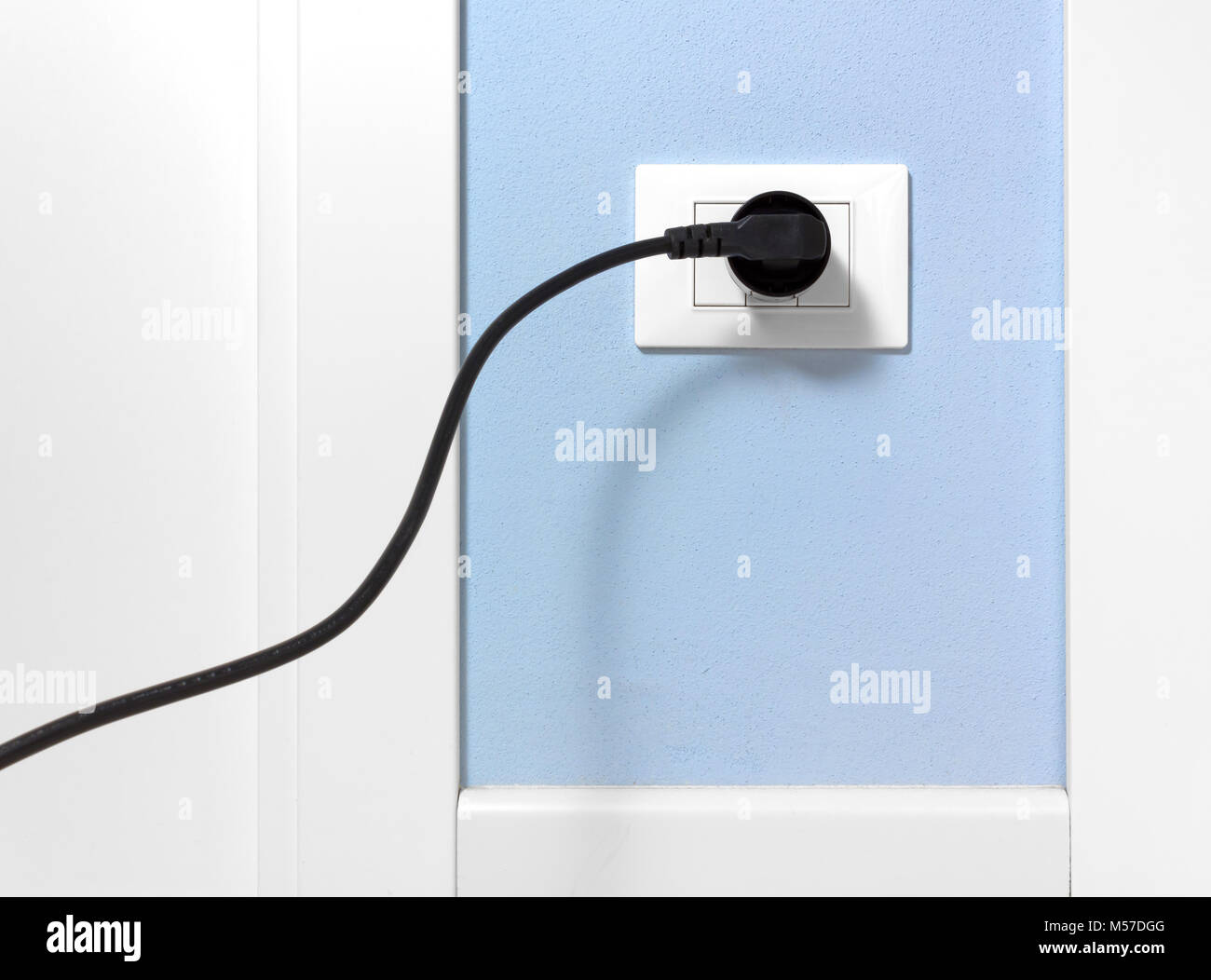 Black plug inserted in a wall socket on a light blue interior wall ...