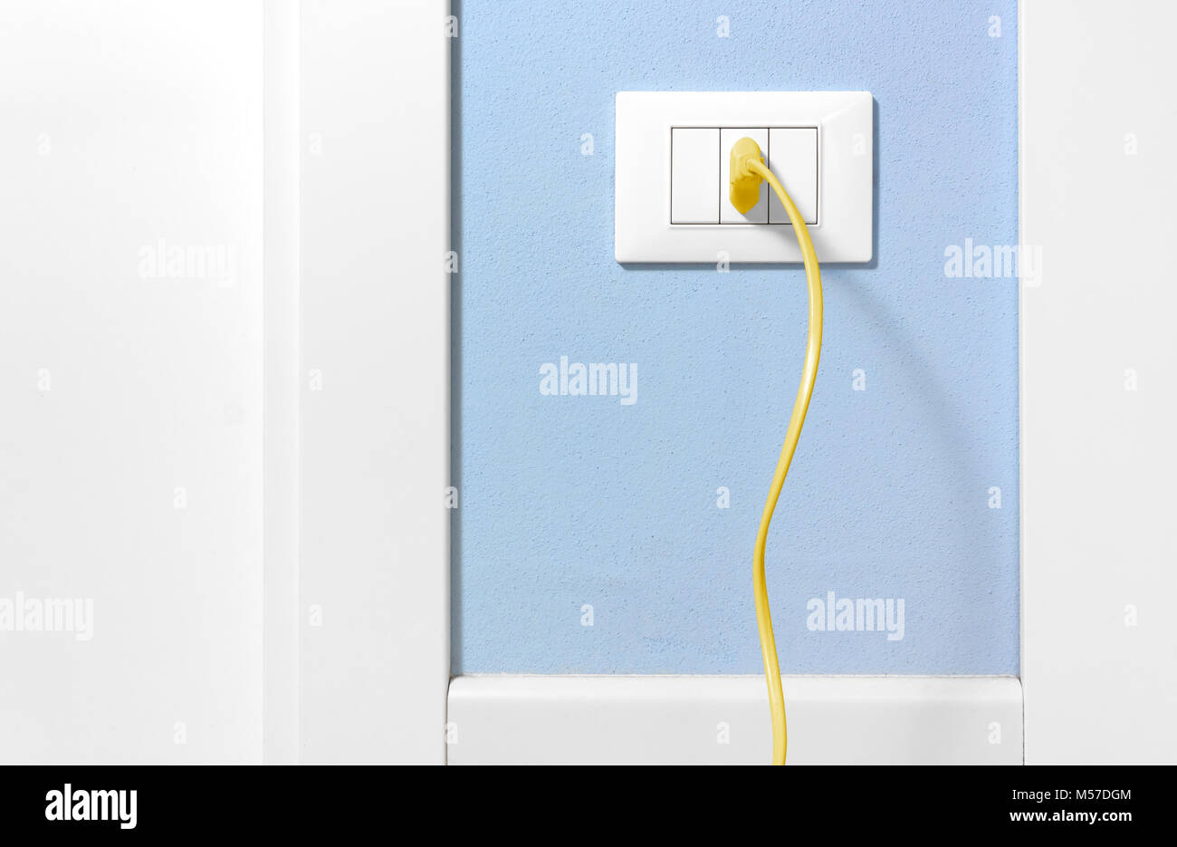 Yellow plug inserted in a wall socket on a light blue interior wall ...