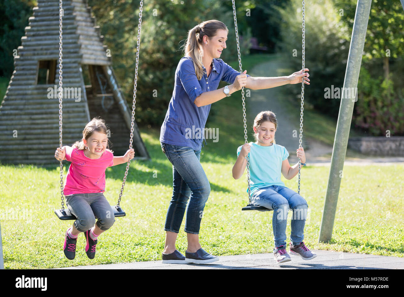Happy family with two girls and mother on playground swing Stock Photo ...