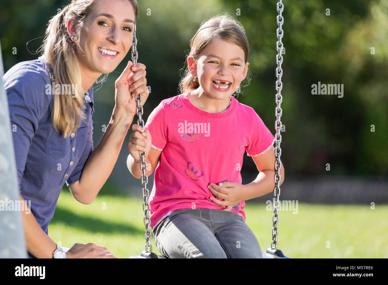 Woman and laughing girl on swing having fun together Stock Photo - Alamy