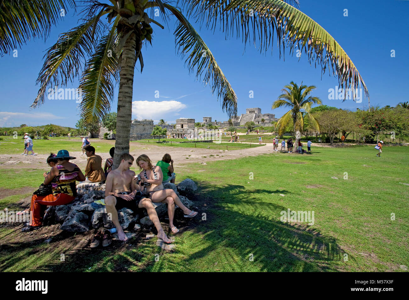 Tourists resting under a palm tree, behind the Mayan ruins ...