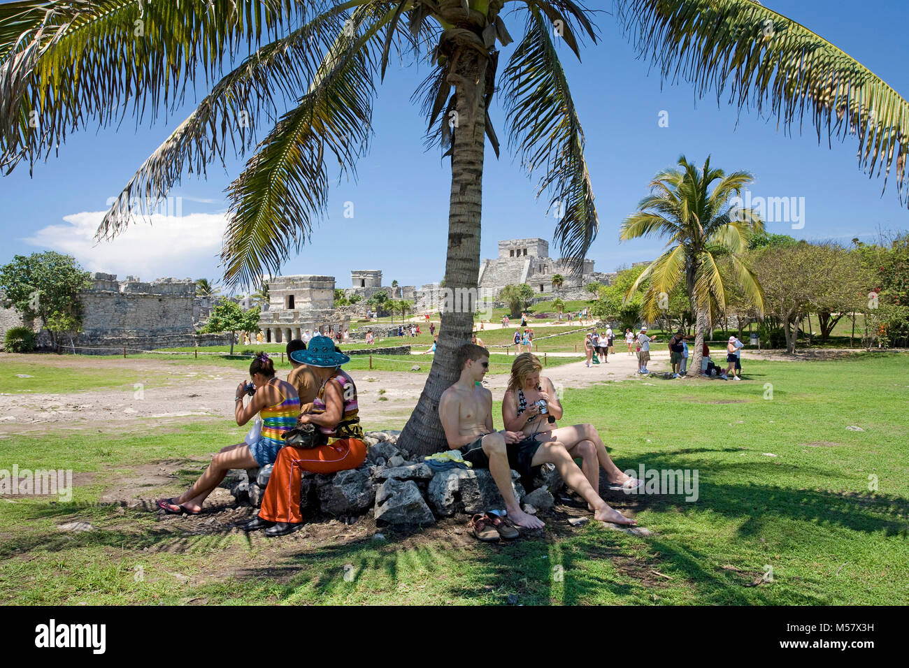 Tourists resting under a palm tree, behind the Mayan ruins ...