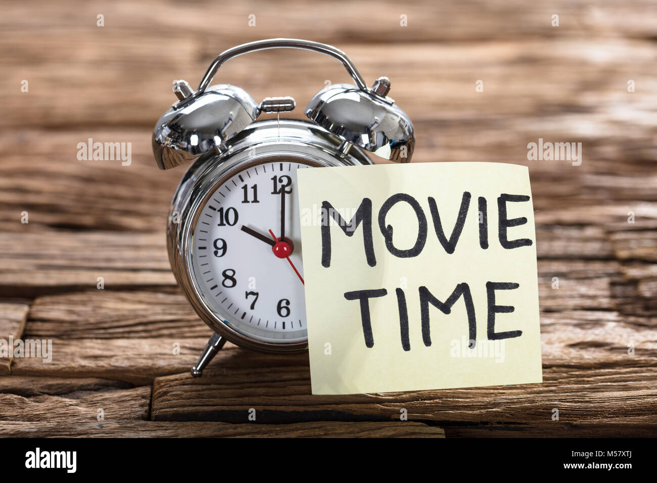 Closeup of alarm clock with movie time text on sticky note on wood ...