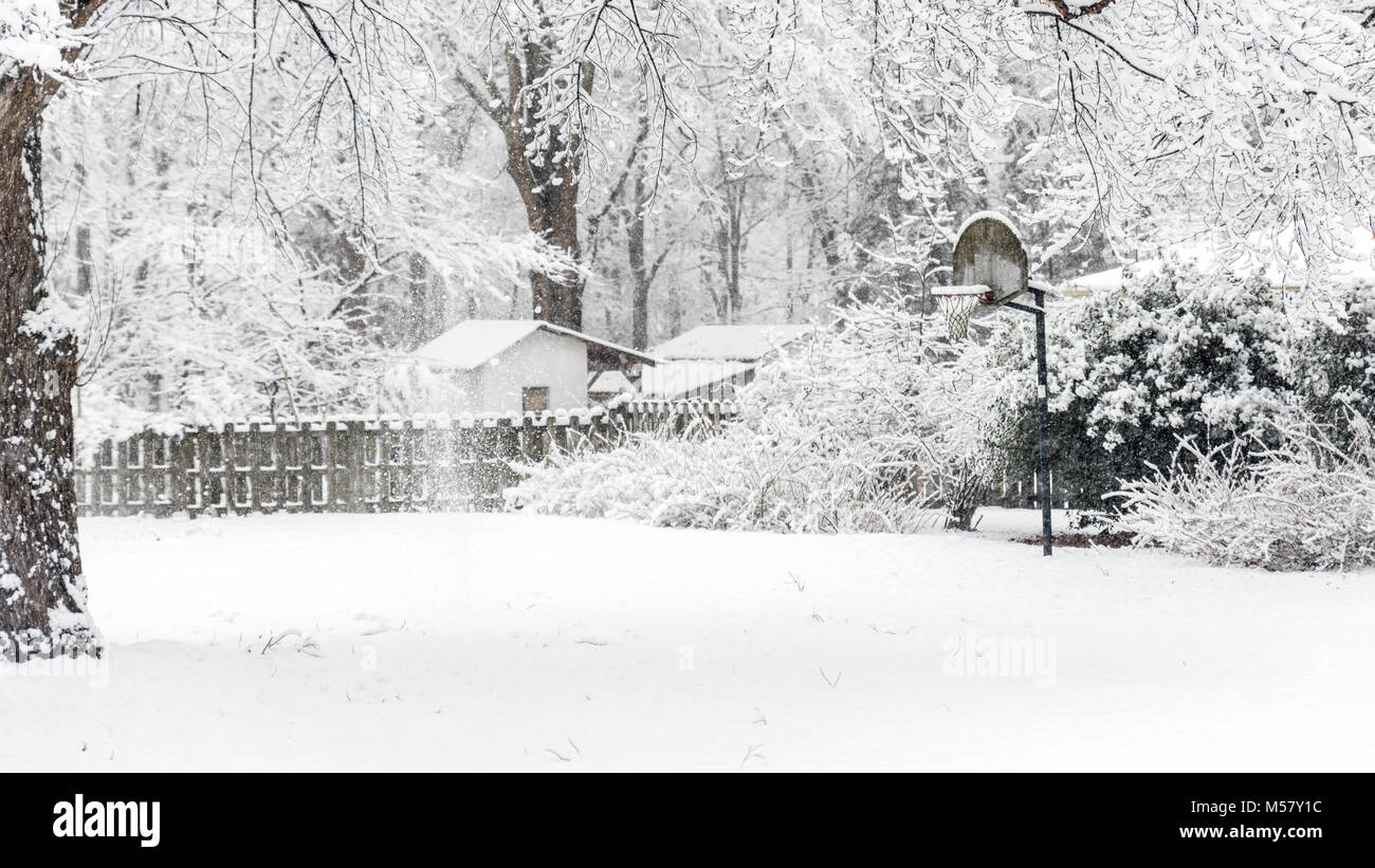 Basketball backboard covered in snow in yard with fence and shack in ...