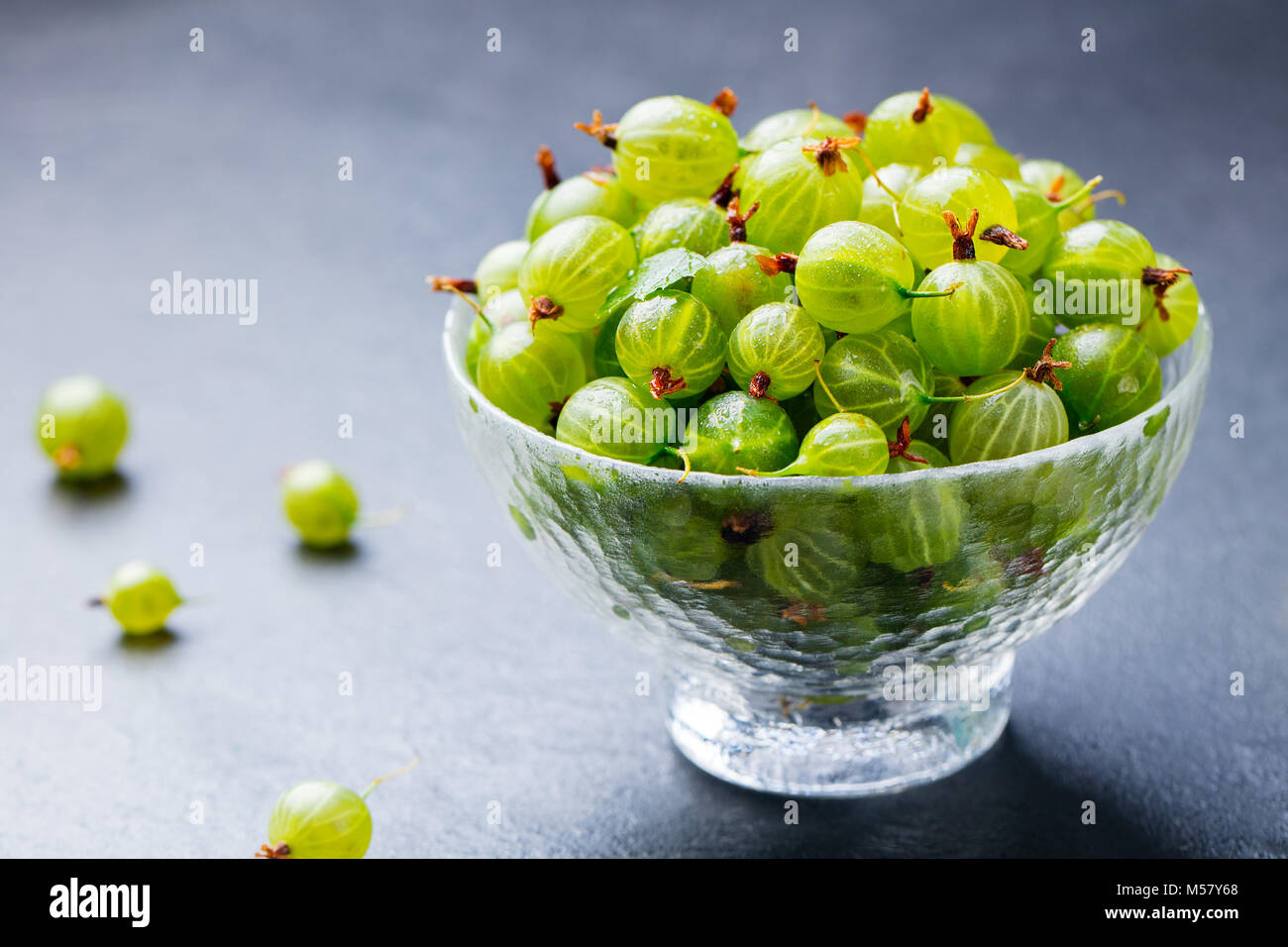 Gooseberries in glass bowl on black stone slate background. Copy space ...