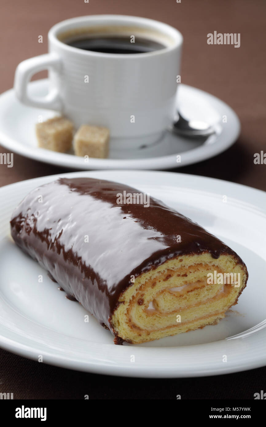 Swiss roll with cream filling and chocolate topping against a cup of ...