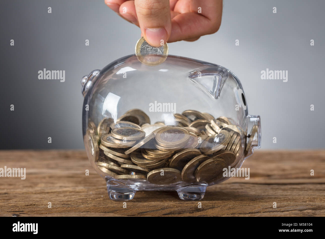 Closeup of hand inserting coin in transparent piggy bank on wooden ...