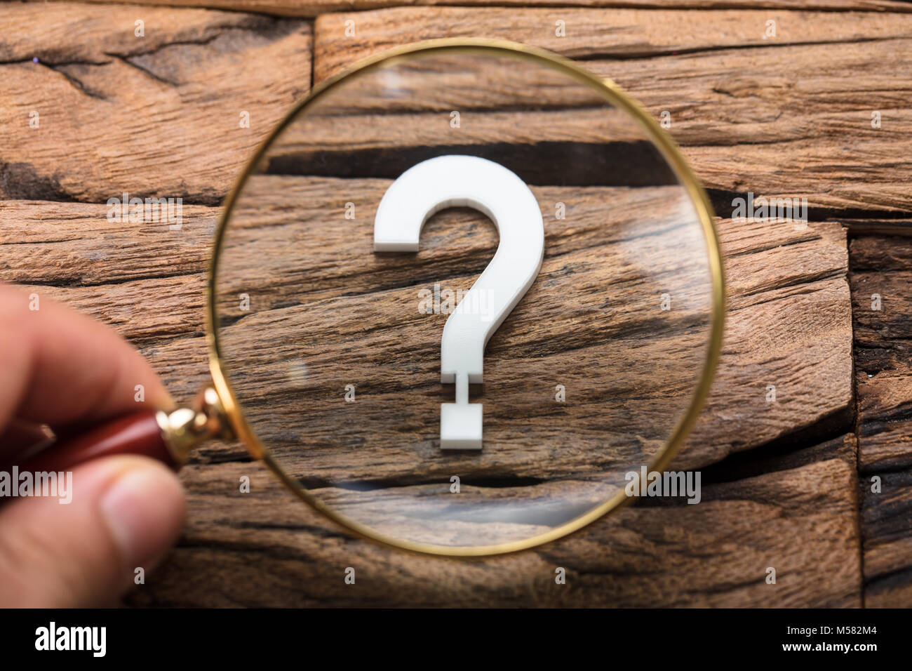 Closeup of hand holding magnifying glass over question mark on wood ...
