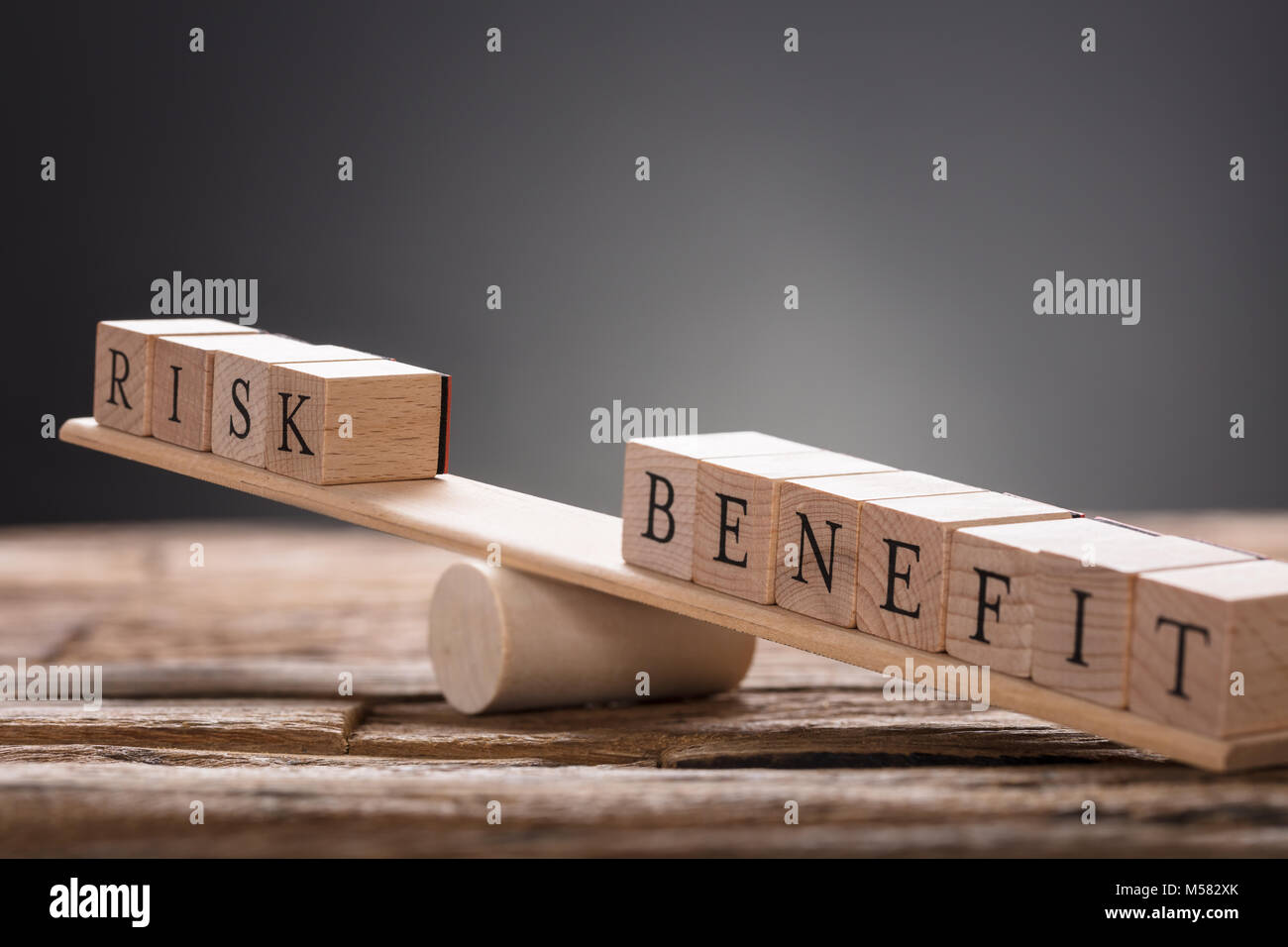 Closeup of risk and benefit wooden blocks on seesaw against gray ...