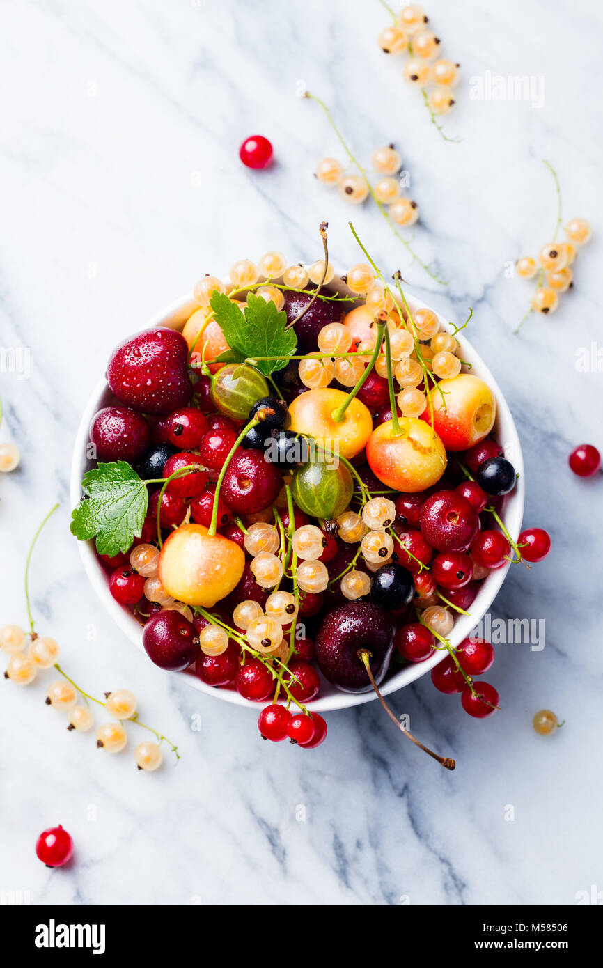 Assortment of fresh berries in white bowl. Marble background. Top view ...