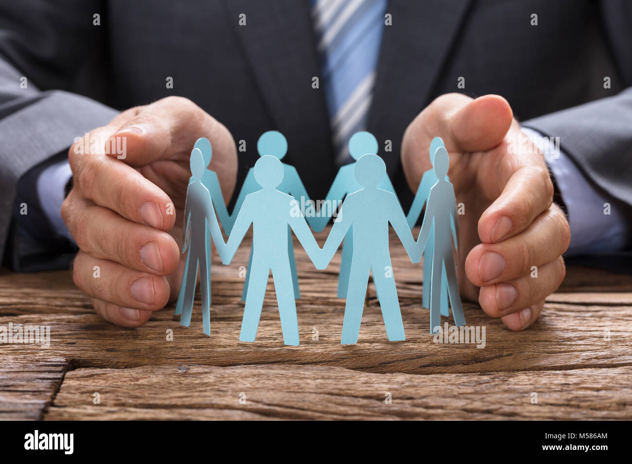 Midsection of businessman covering paper team with hands on wooden ...