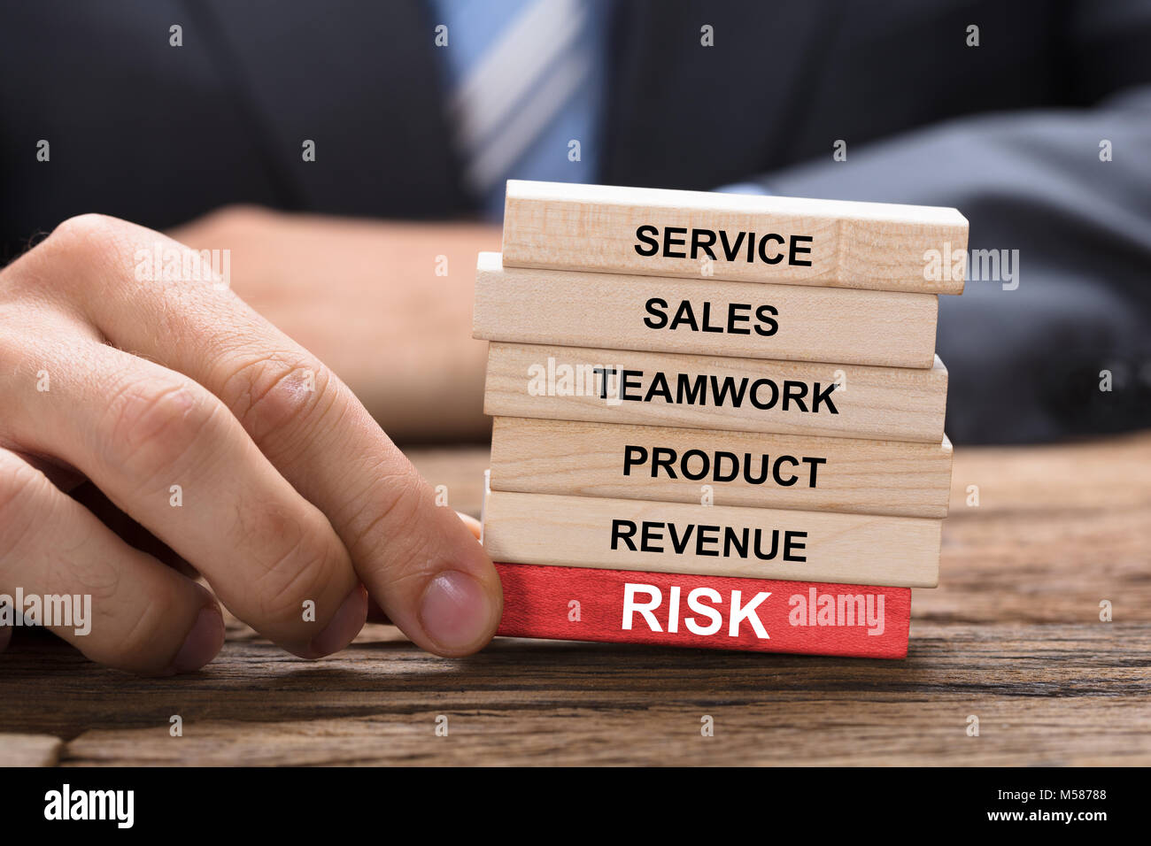 Cropped image of businessman holding red risk block under wooden tower ...