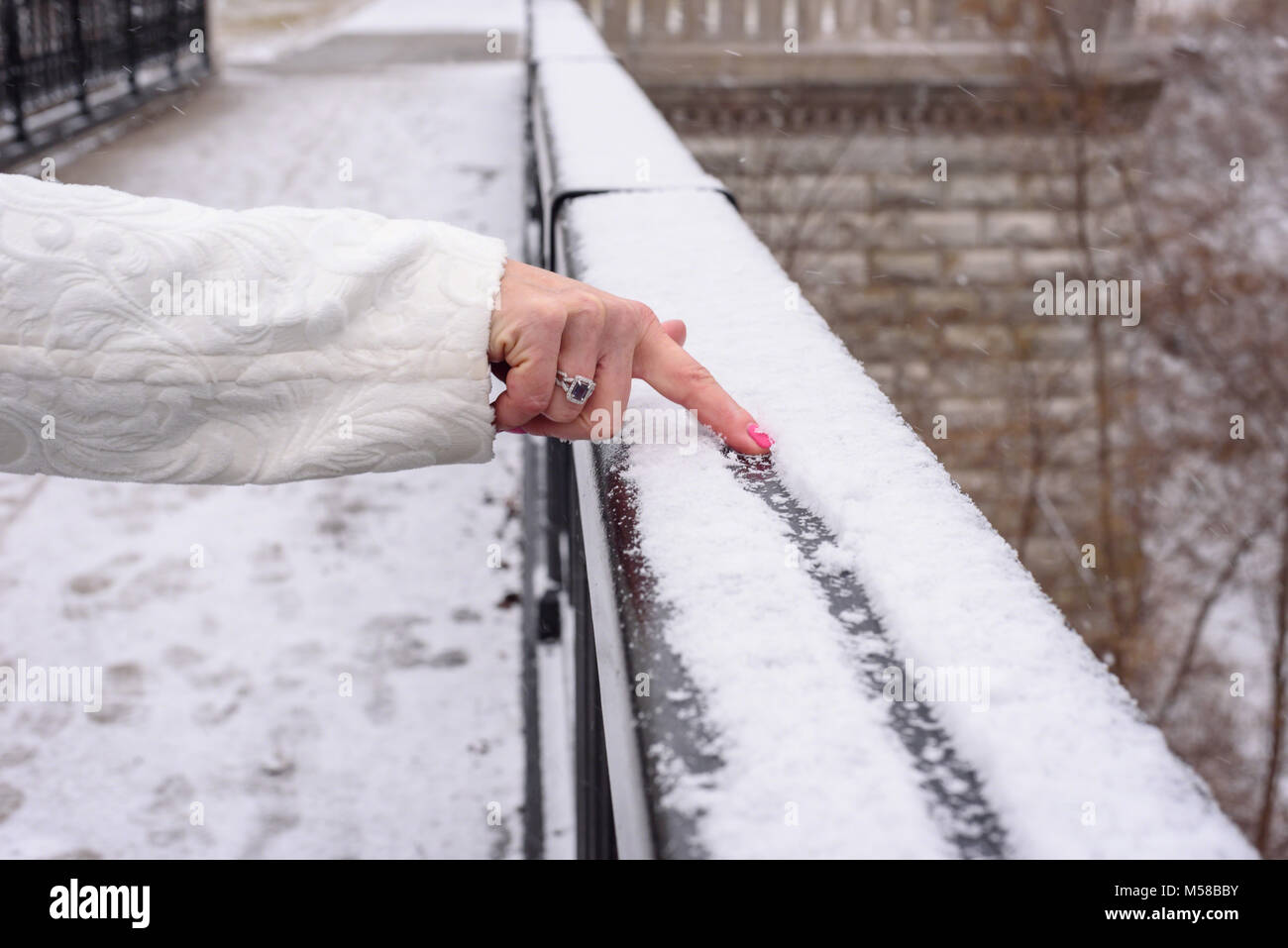 closeup of womans hand drawing a line in fresh snow on railing in city ...
