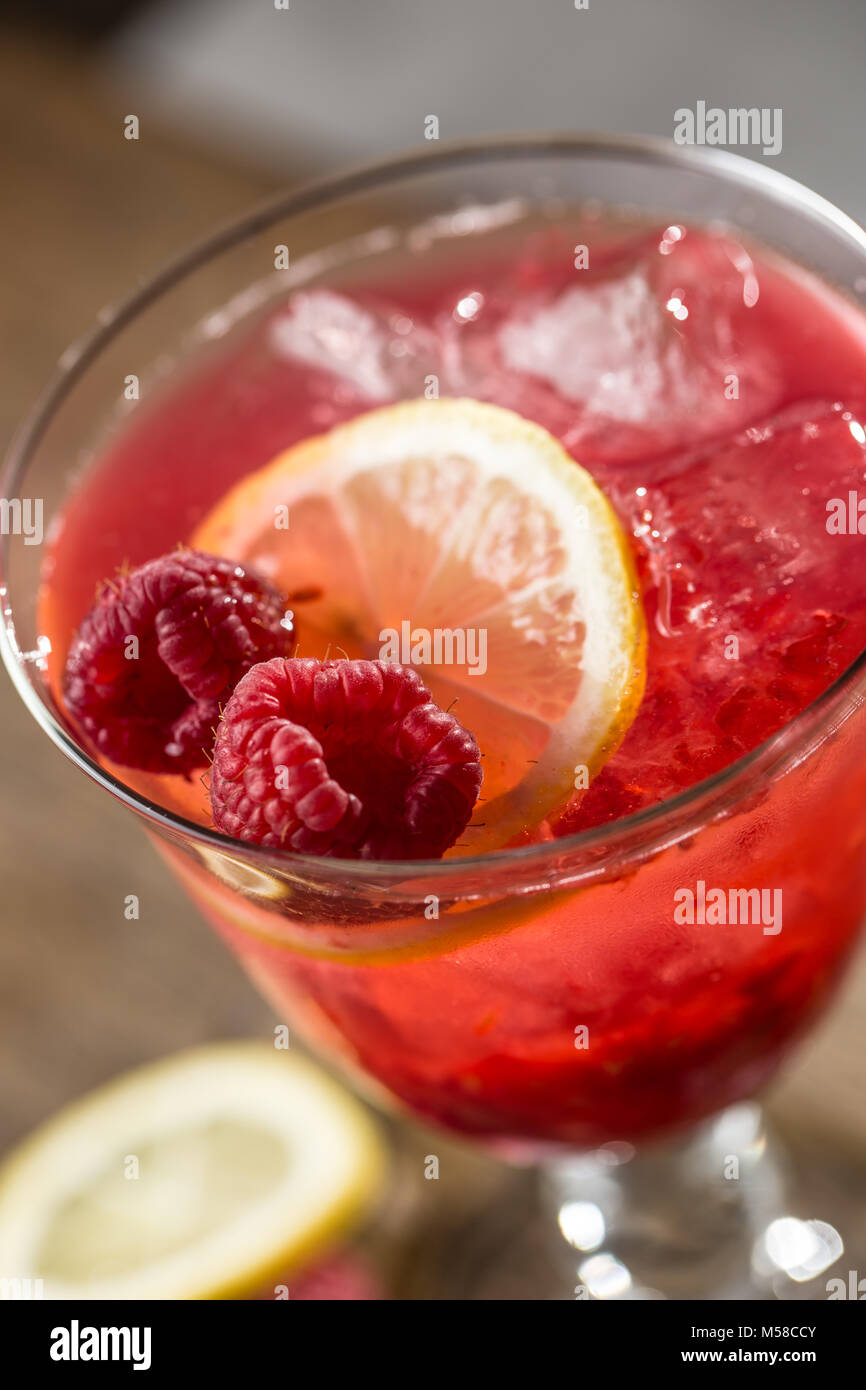 Alcoholic beverage with raspberries lemon and ice on bar counter in pub ...