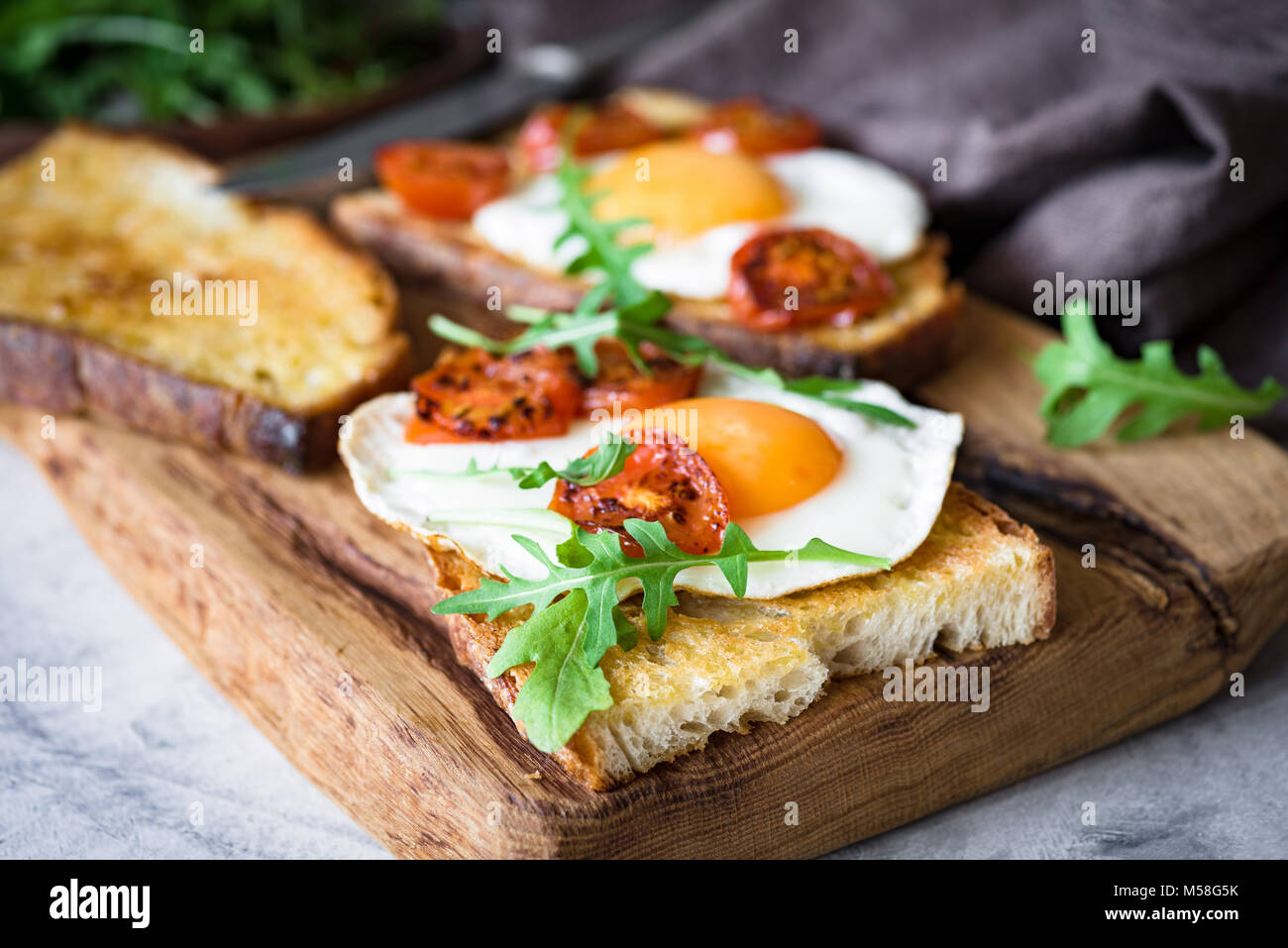 Healthy breakfast toast with egg, roasted tomato and arugula on rustic ...