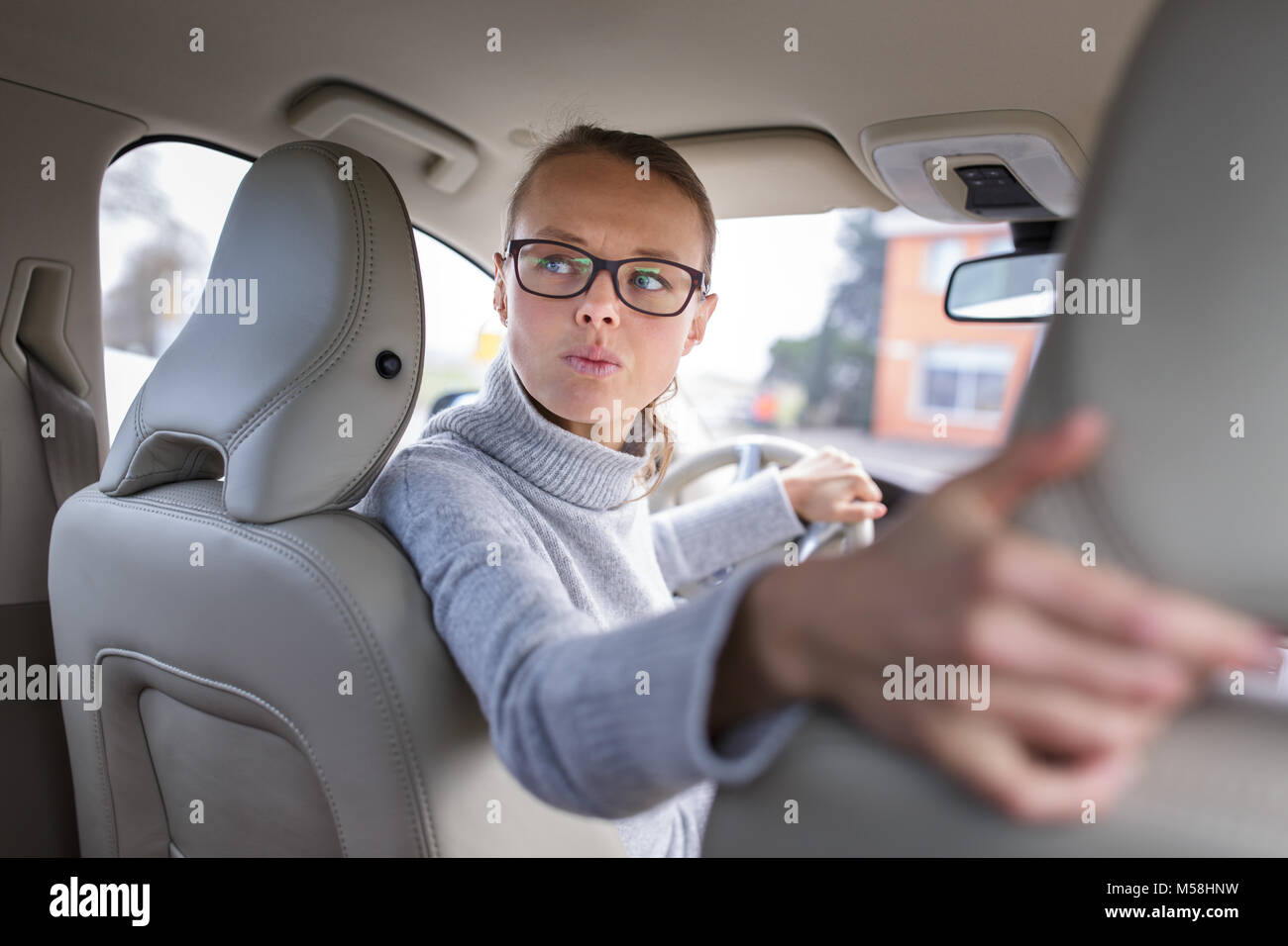 Pretty, young woman driving her new car -going in reverse, being quite ...