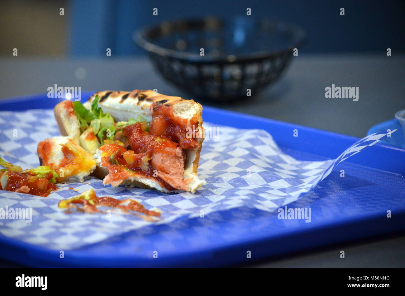 Detail of a messy hot dog bun with condiments on a blue tray in a fast ...