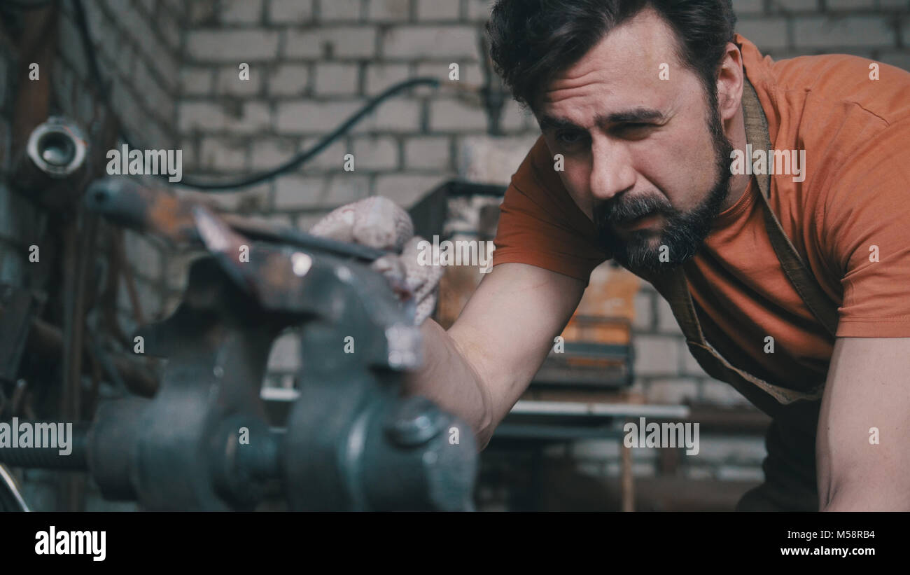 Blacksmith bends metal knife with gripe in workshop forge, portrait ...