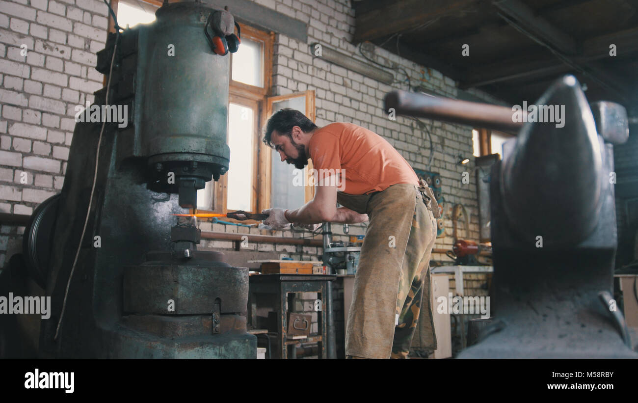 Man blacksmith forges the metal at the mechanical hammer Stock Photo ...