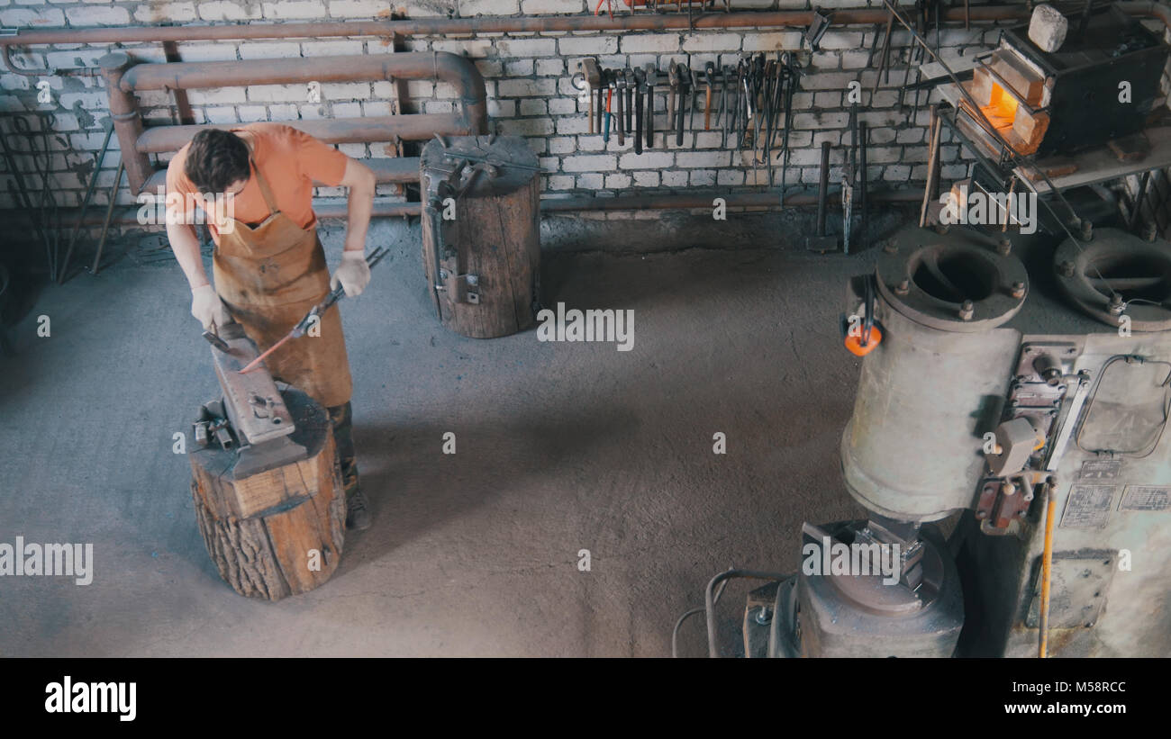 Beard man blacksmith in forge makes metal tools on iron anvil with ...