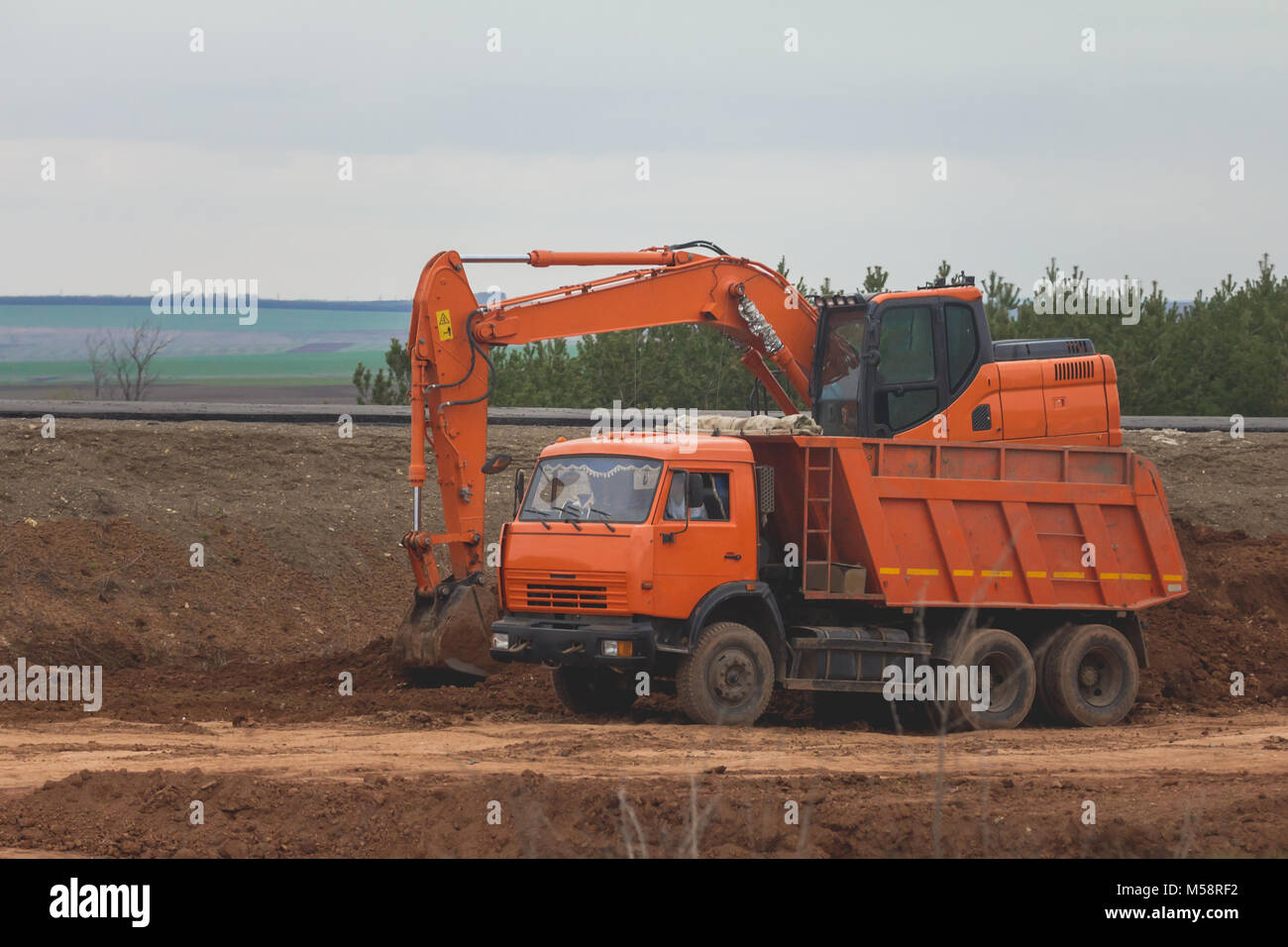 Heavy excavator loading dumper truck on road construction among fields ...