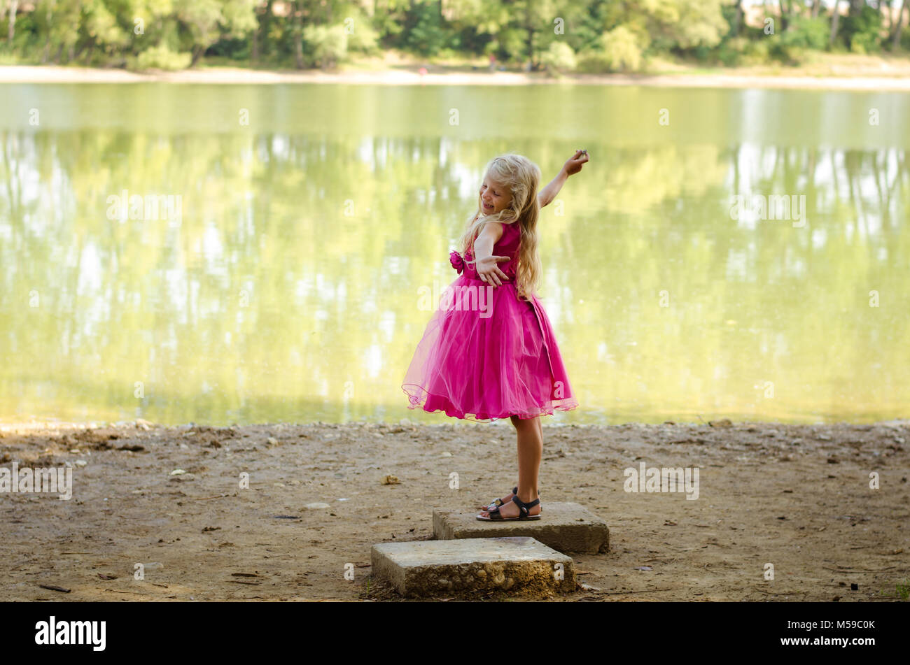 adorable blond girl jumping in the strand of the lake Stock Photo - Alamy