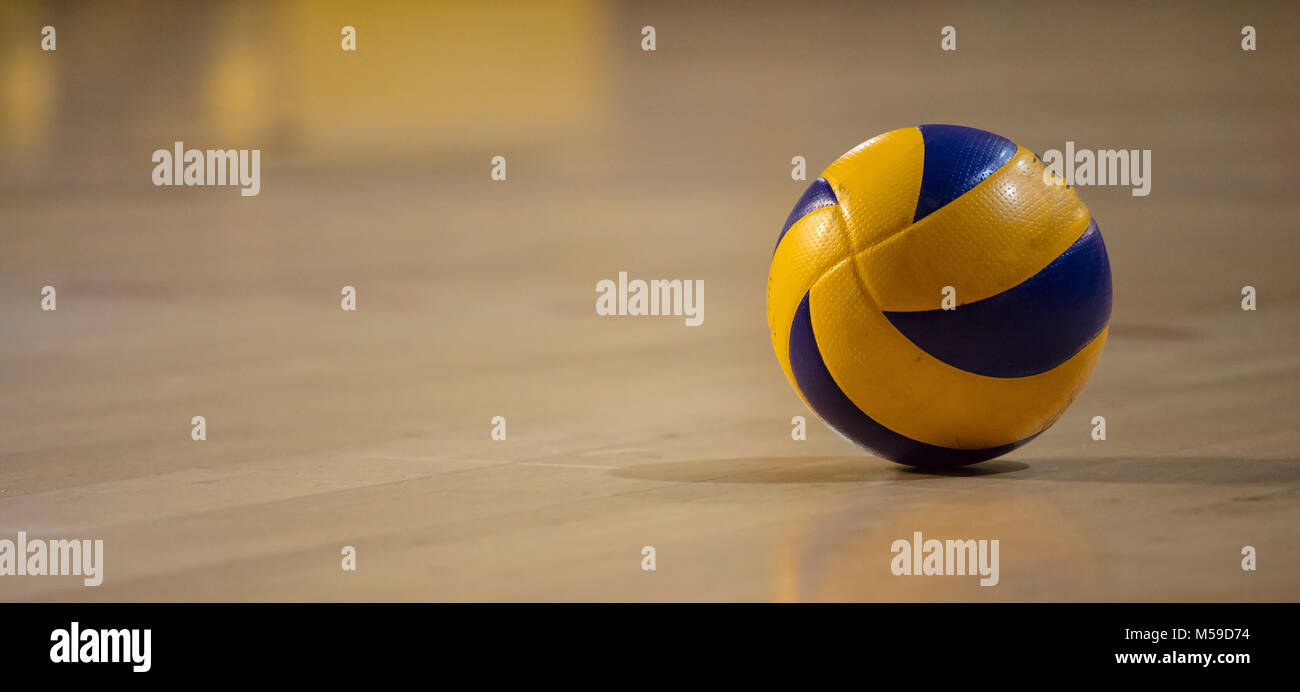 Volleyball ball, blue-yellow, with reflection. Blurred wooden parquetry ...