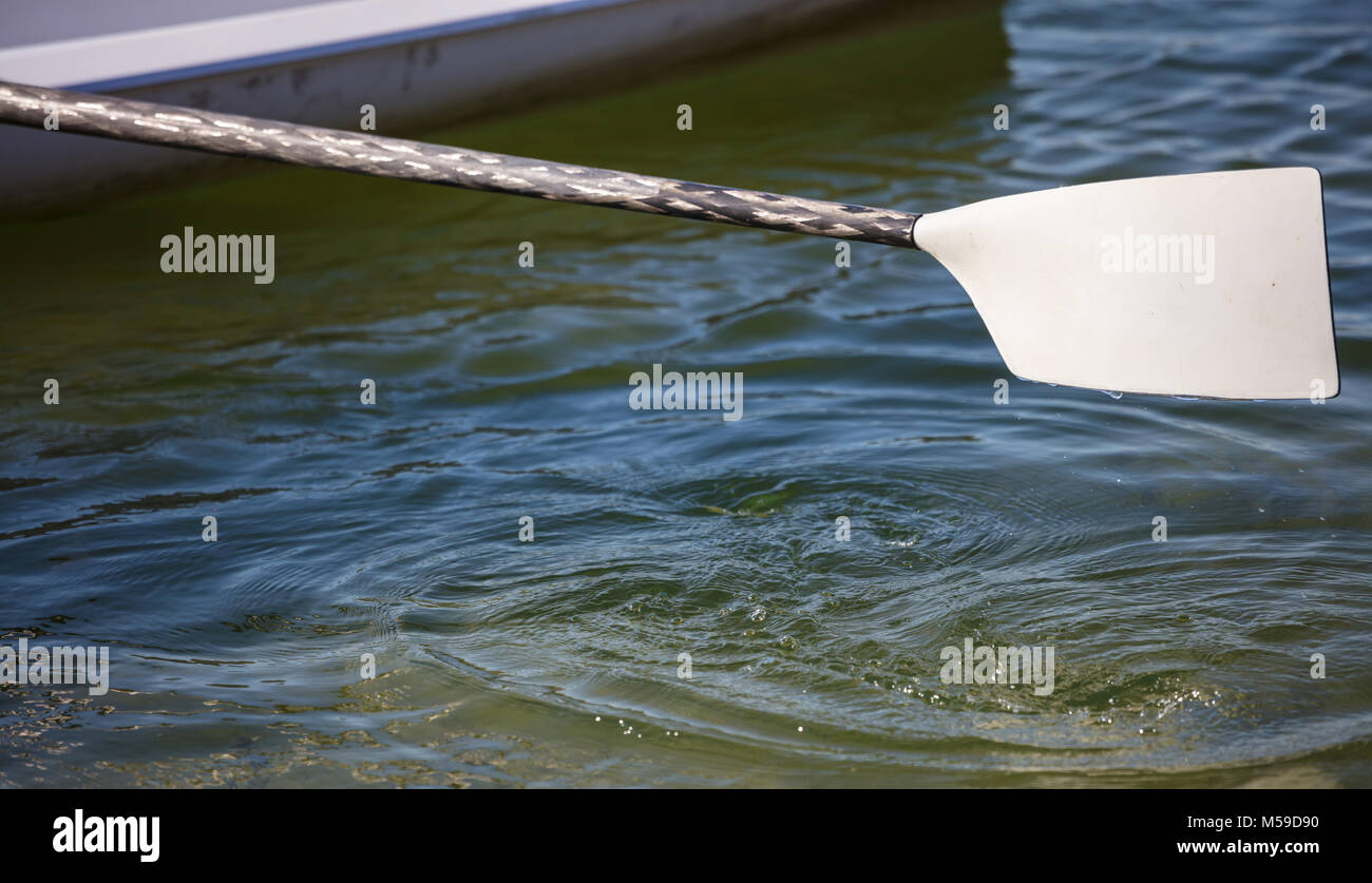 A side of boat and a white oar ready to touch the swirl sea. Blue sea ...