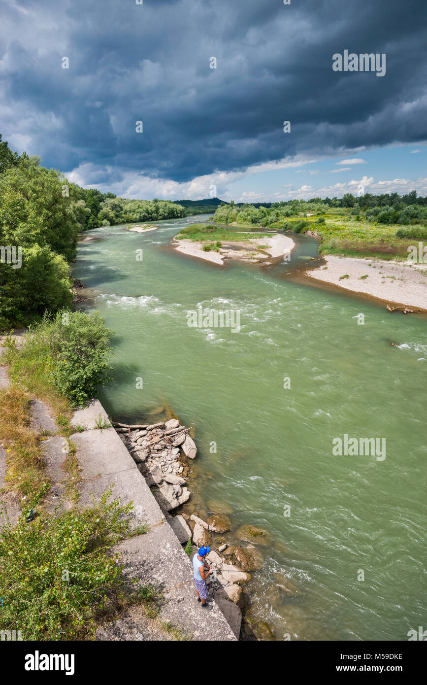 Man fishing in Prut river under dark clouds seen from highway bridge ...