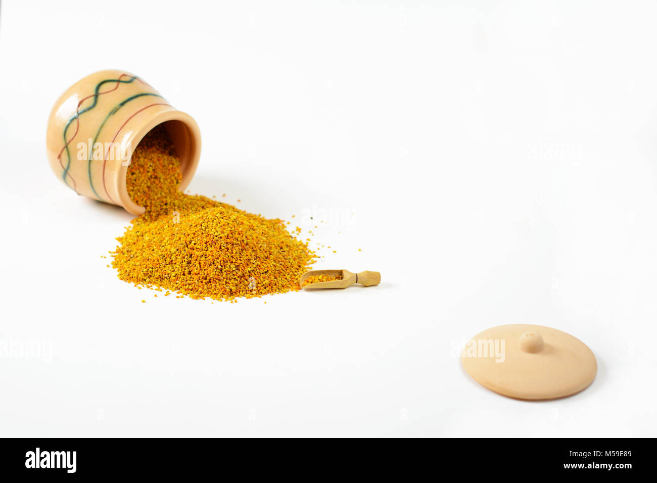 Bee pollen poured out from a small glazed clay pot. Next to the pile of ...