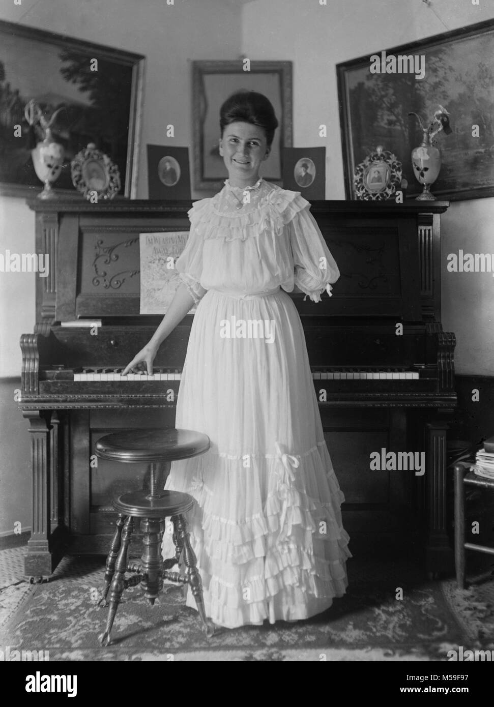 A smiling piano teacher awaits her students, ca. 1904 Stock Photo - Alamy