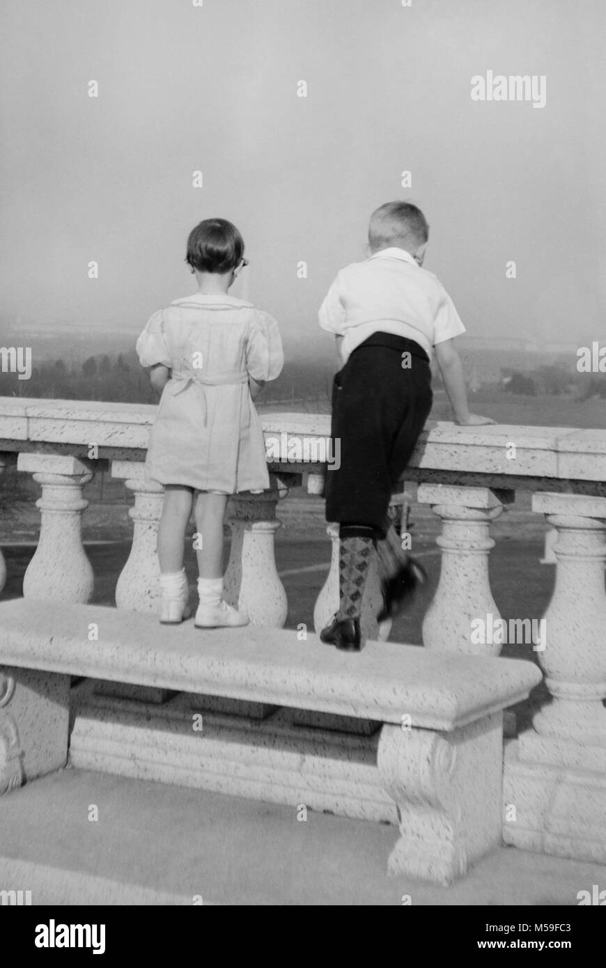 Rear view of two children looking over a railing, ca. 1950 Stock Photo ...