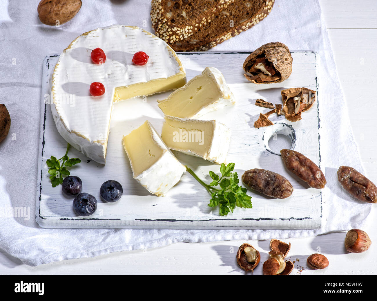 round Camembert cheese on a white wooden board, next to sausage and ...