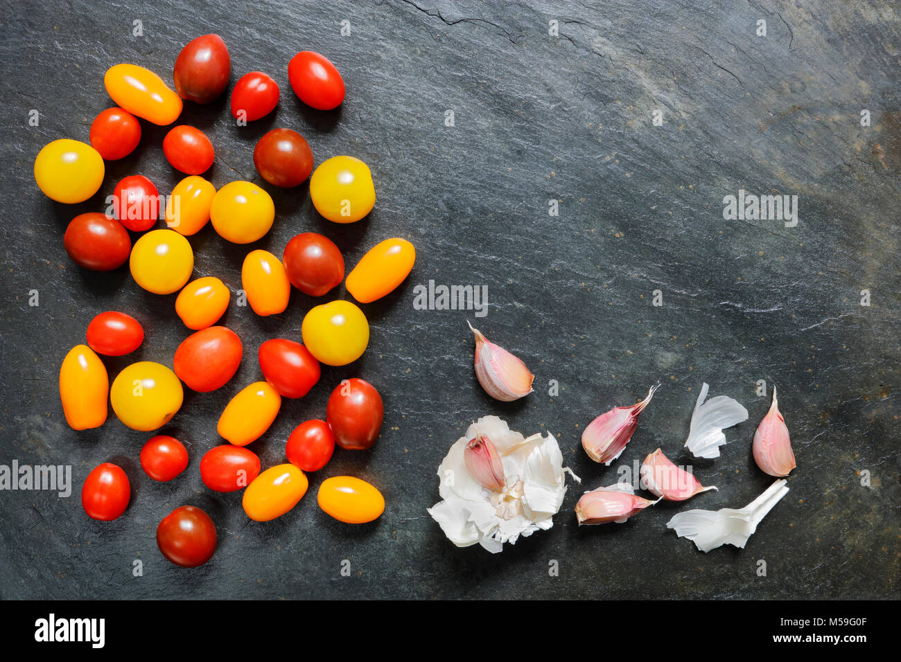 Assorted red, dark, yellow and orange small cherry tomatoes with garlic ...