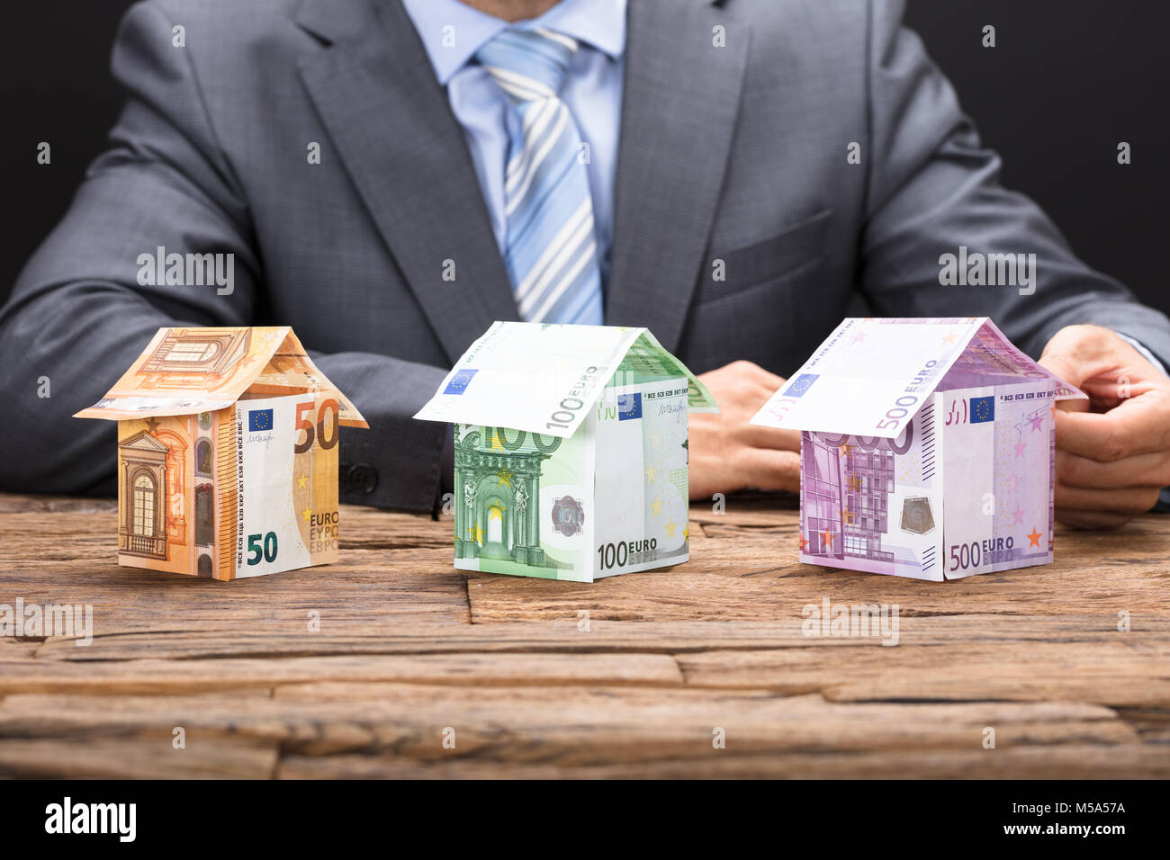 Businessman making houses from euro paper currencies on wooden table ...