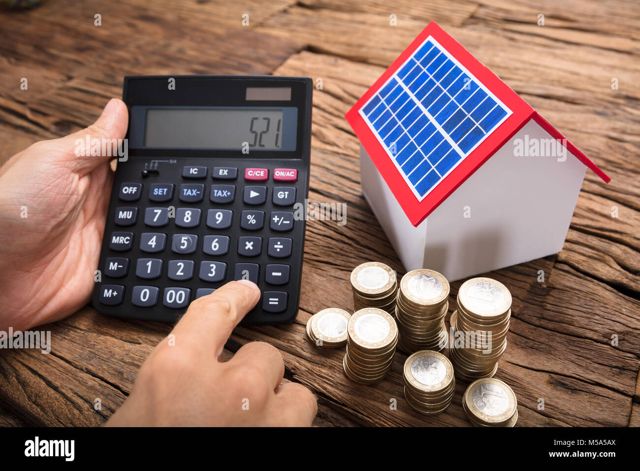 Businessman using calculator by coins and model home with solar panel ...
