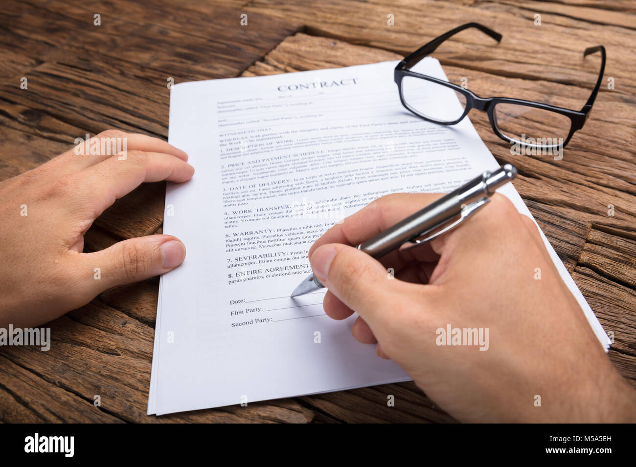 Cropped hands of businessman signing contract at wooden table Stock ...