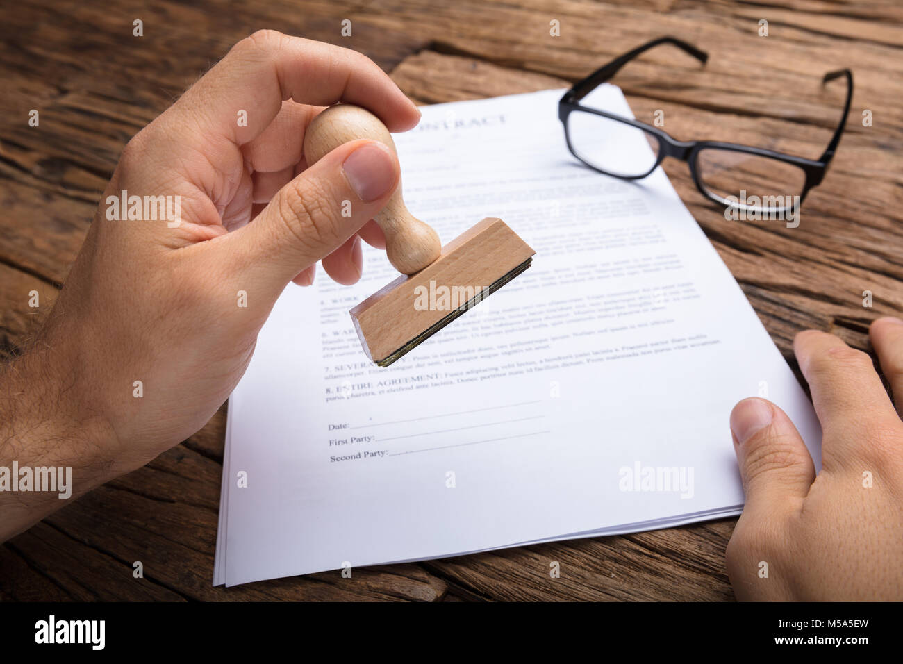 Cropped hands of businessman stamping contract paper at wooden table ...
