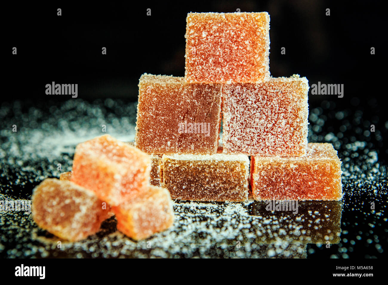 Pyramid of orange marmelade coated with sugar on black mirror ...